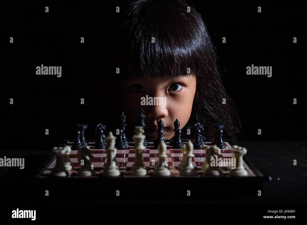 Asian Little Chinese girl playing chess in isolated black background ...