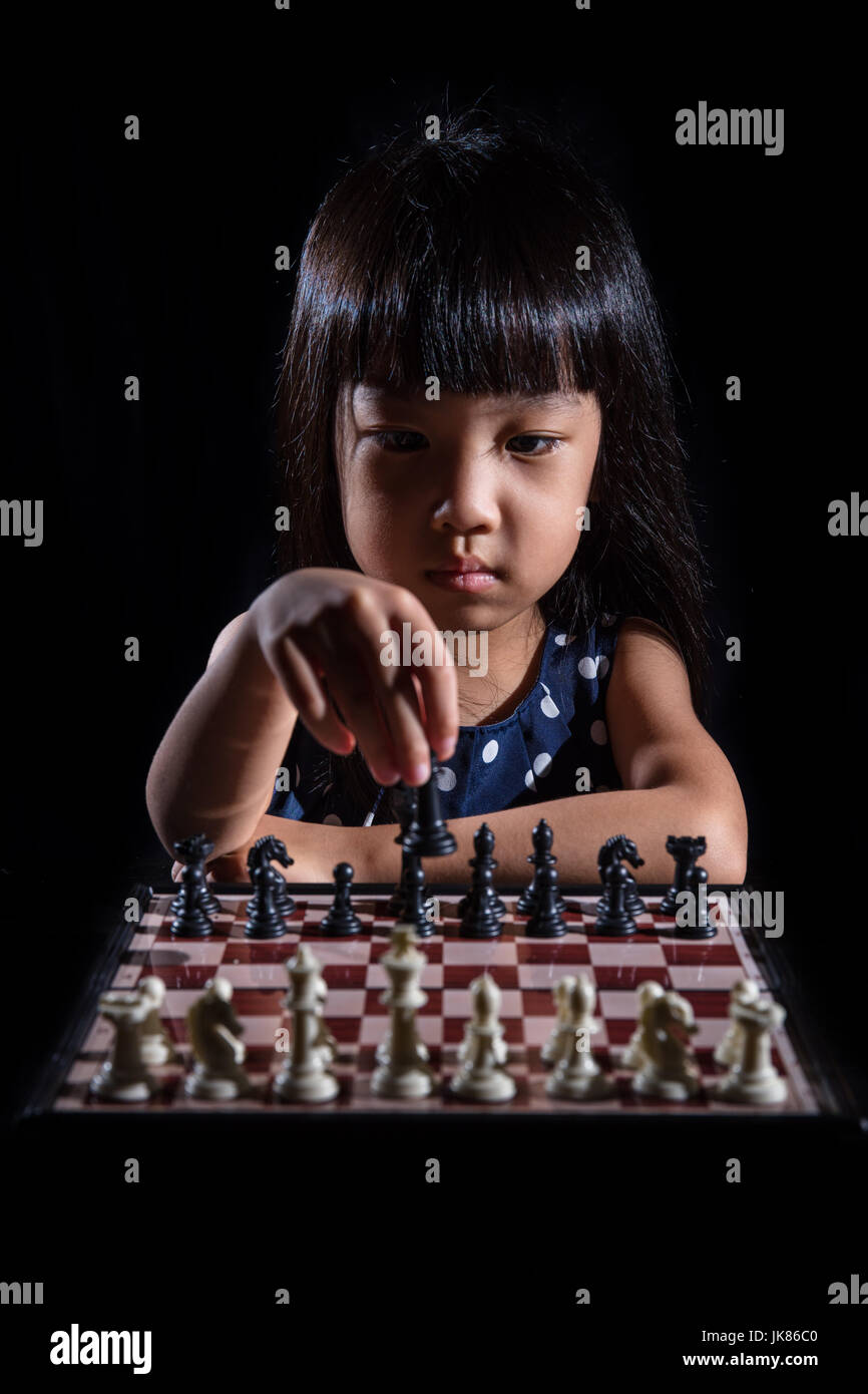 Asian Little Chinese girl playing chess in isolated black background ...