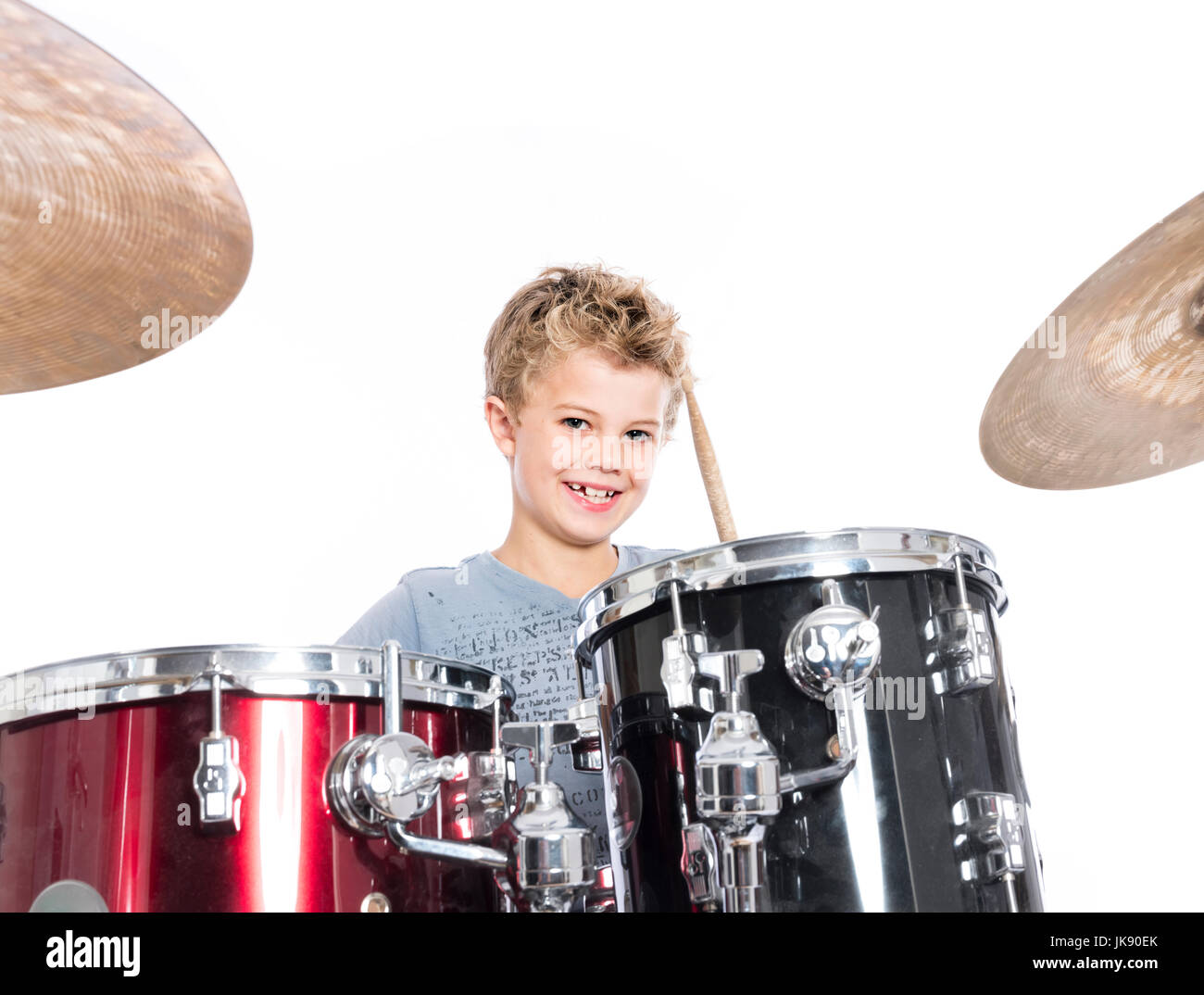 young blond caucasian boy plays drums in studio against white ...