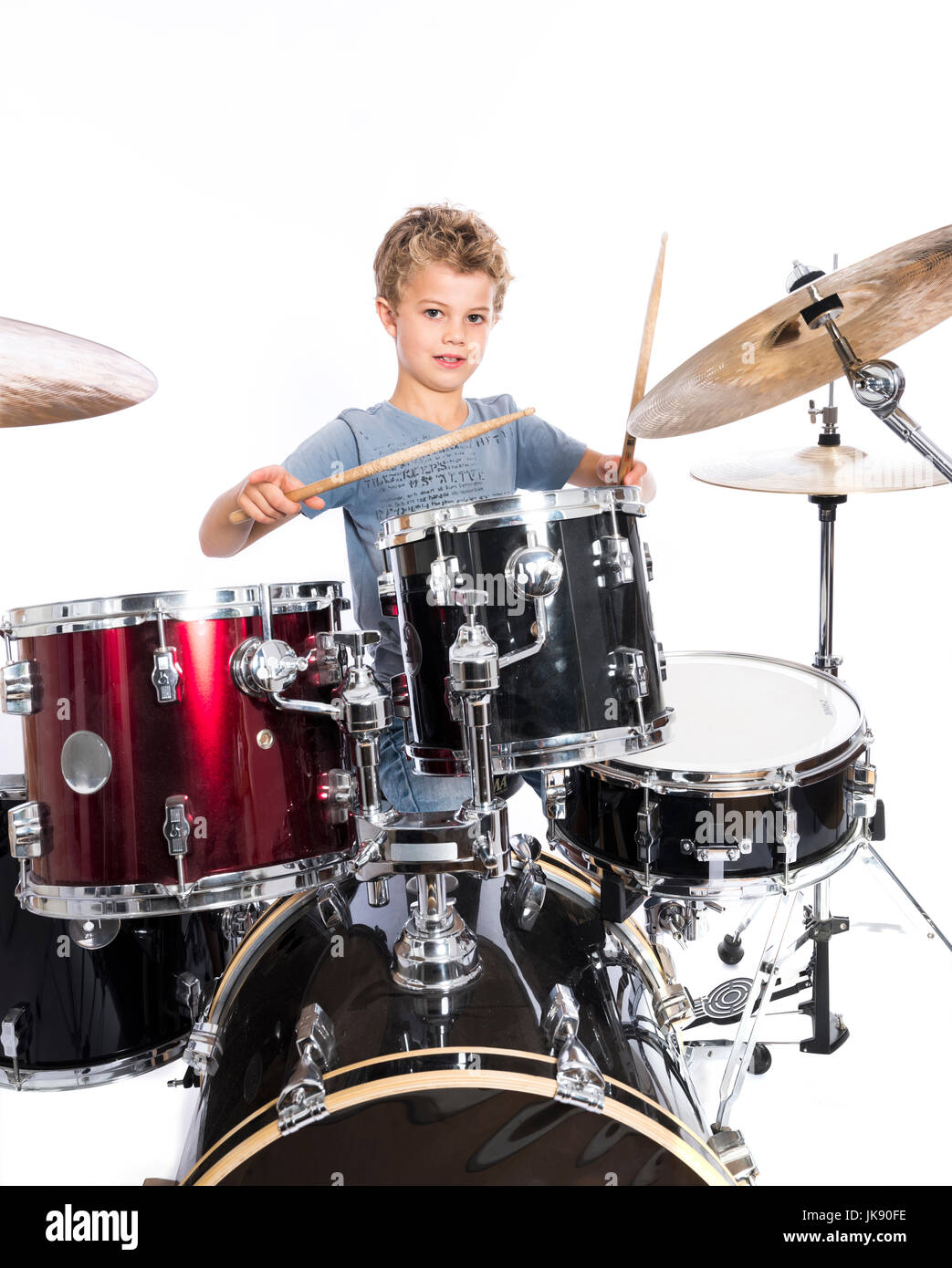 young blond caucasian boy plays drums in studio against white ...