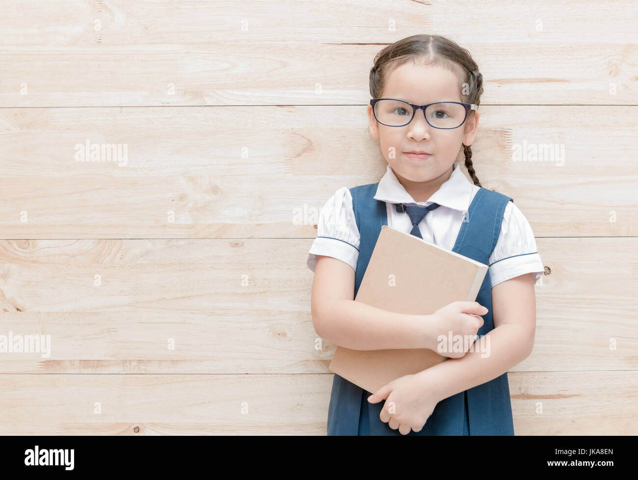 Happy cute girl student in uniform with book on wood background ...