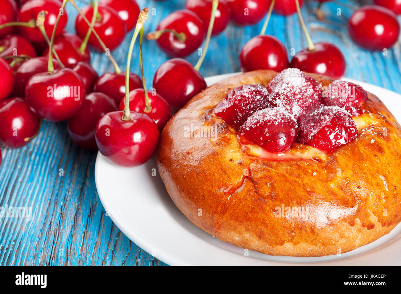 Fresh homemade bun with sweet cherry in a white dish on a blue wooden ...