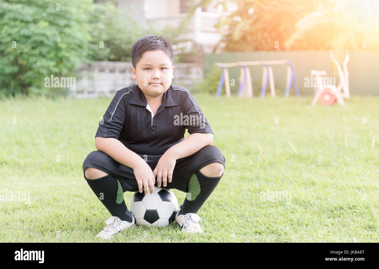 obese fat boy soccer player sit on football and green grass background ...