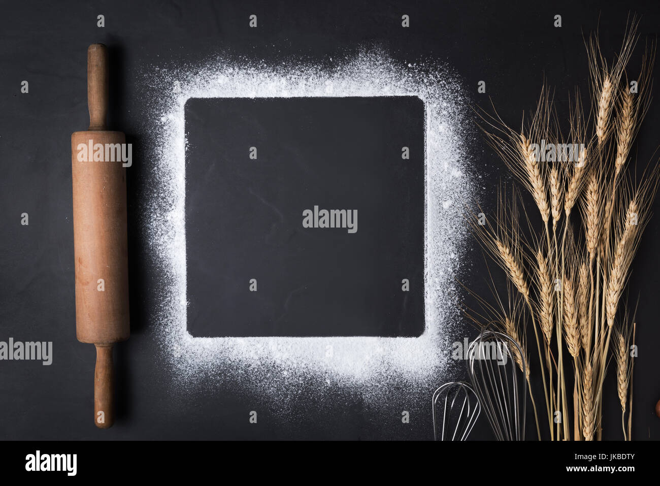 Baking utensils and flour with whisk and rolling pin on black ...