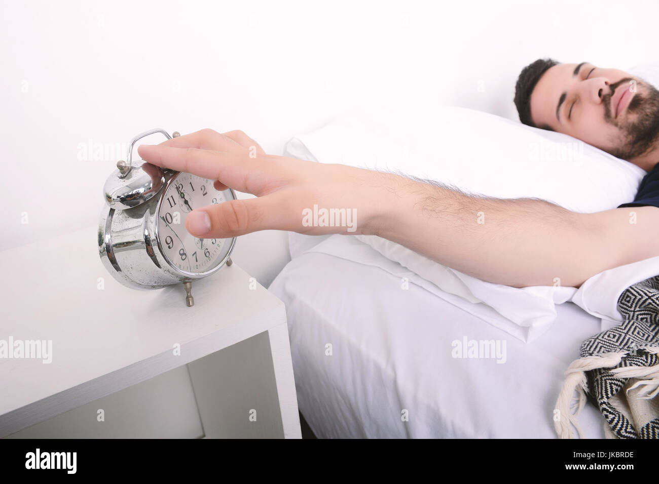 Attractive young man turning off the alarm clock. Indoors Stock Photo ...
