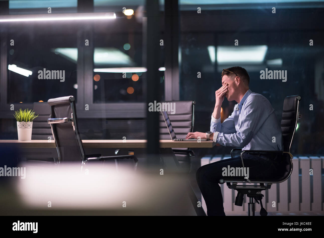 Young man working on laptop at night in dark office. The designer works ...