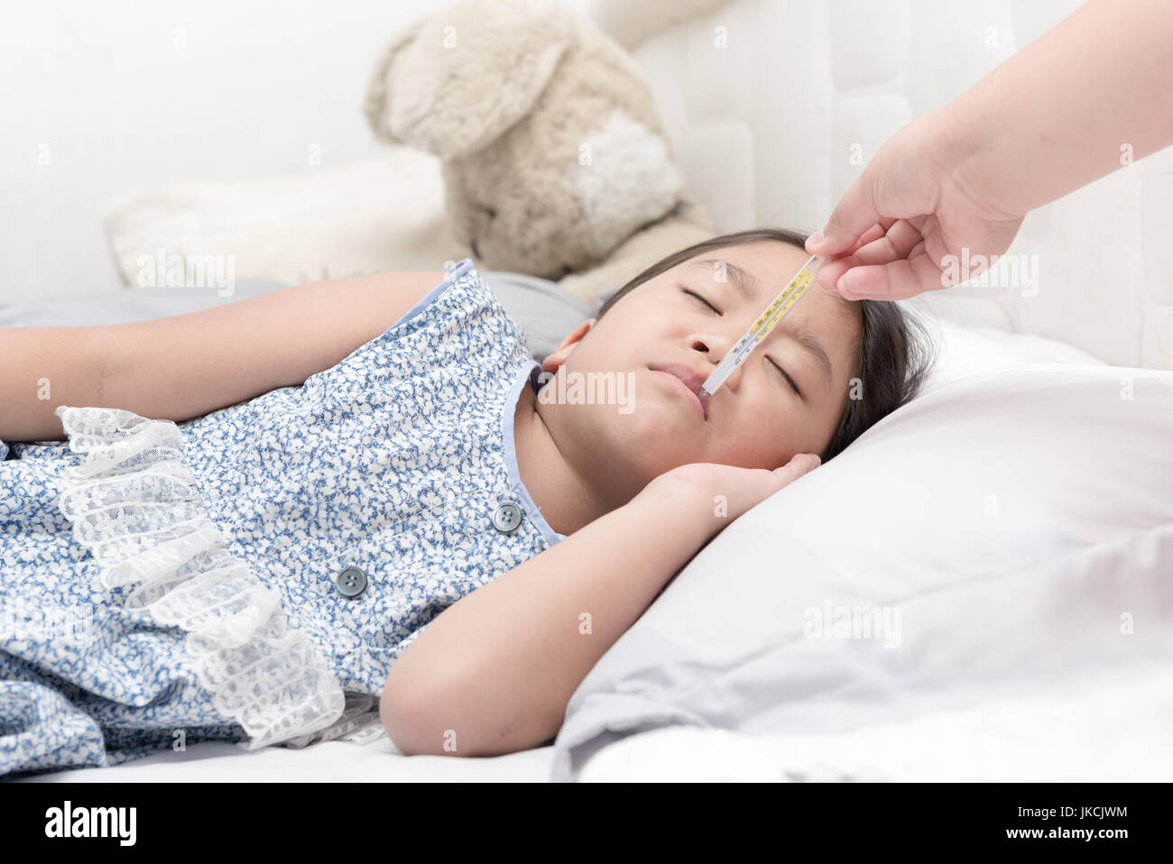 Mother measuring temperature of her ill kid. Sick child with high fever laying in bed and mother ...