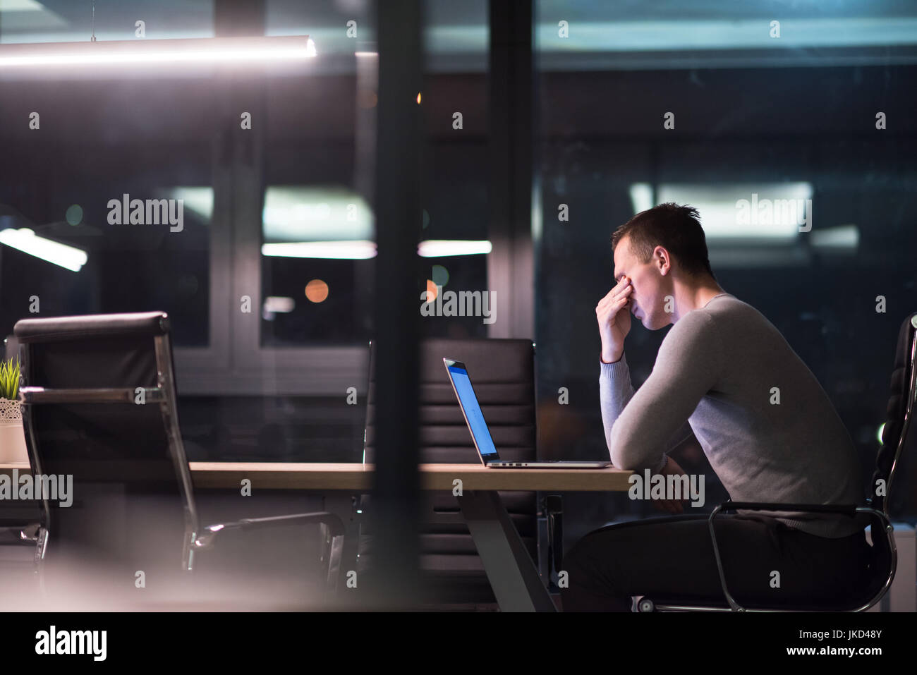 Young man working on laptop at night in dark office. The designer works ...