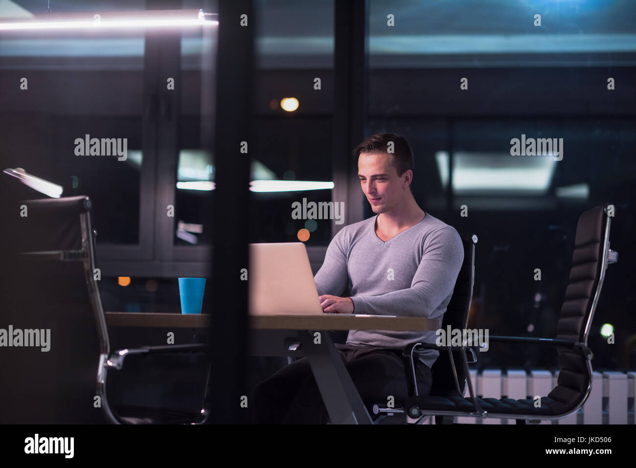 Young man working on laptop at night in dark office. The designer works ...