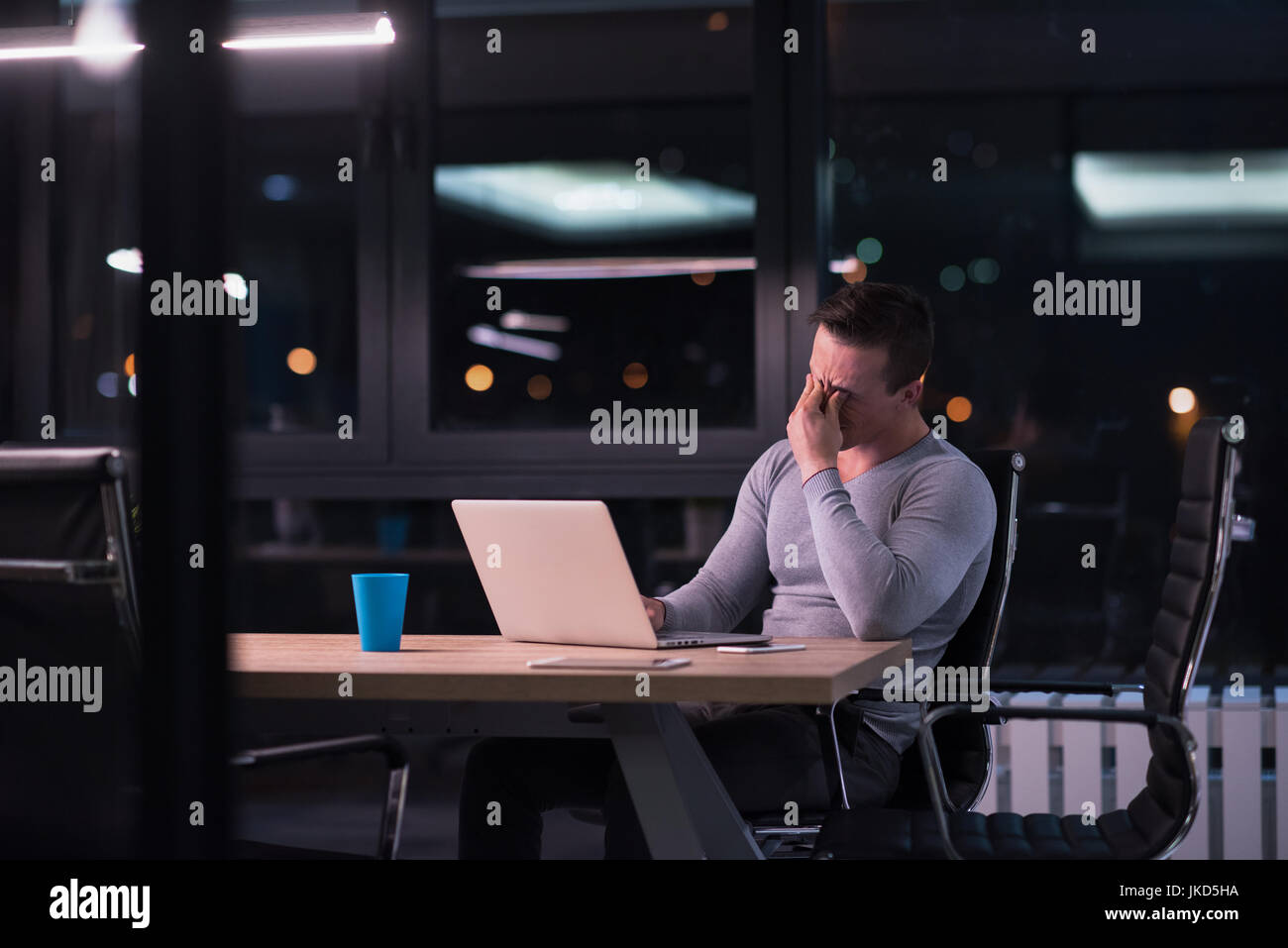 Young man working on laptop at night in dark office. The designer works ...