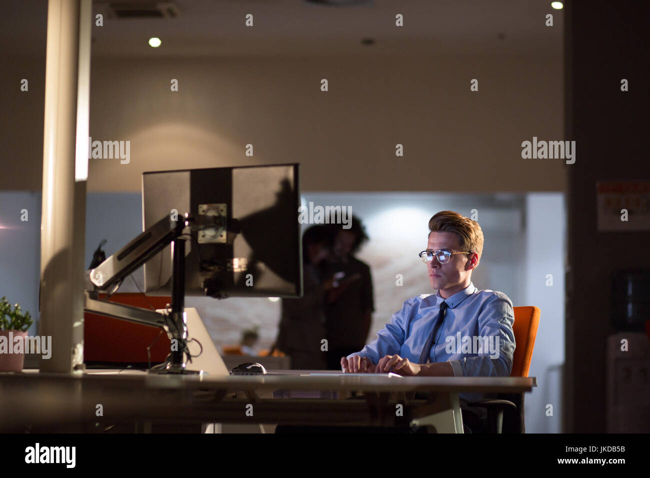 Young man working on computer at night in dark office. The designer ...