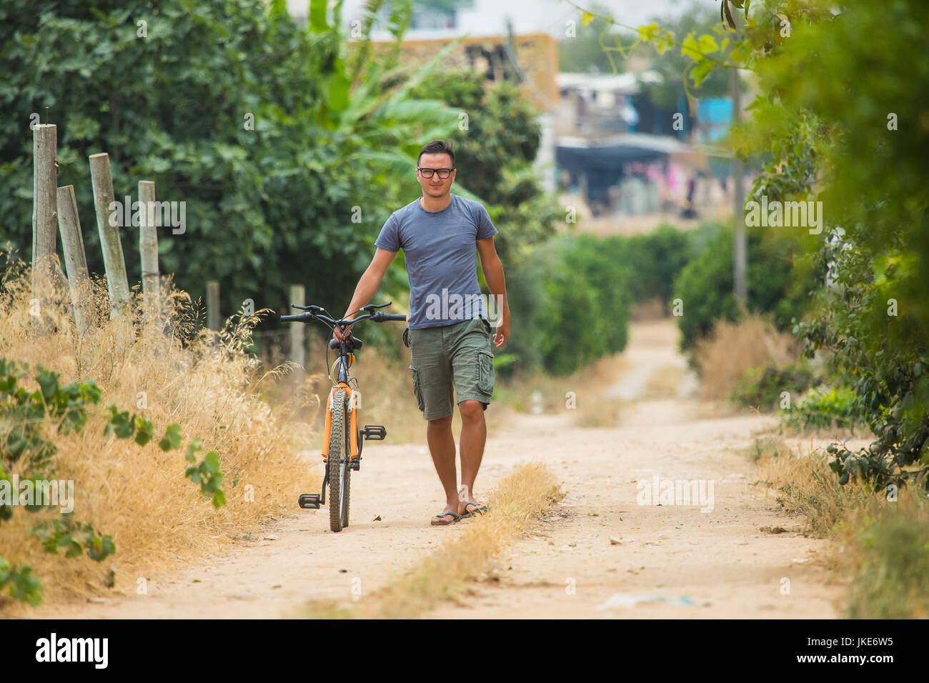 Time for a cycle handsome young smiling man walking along a road with ...