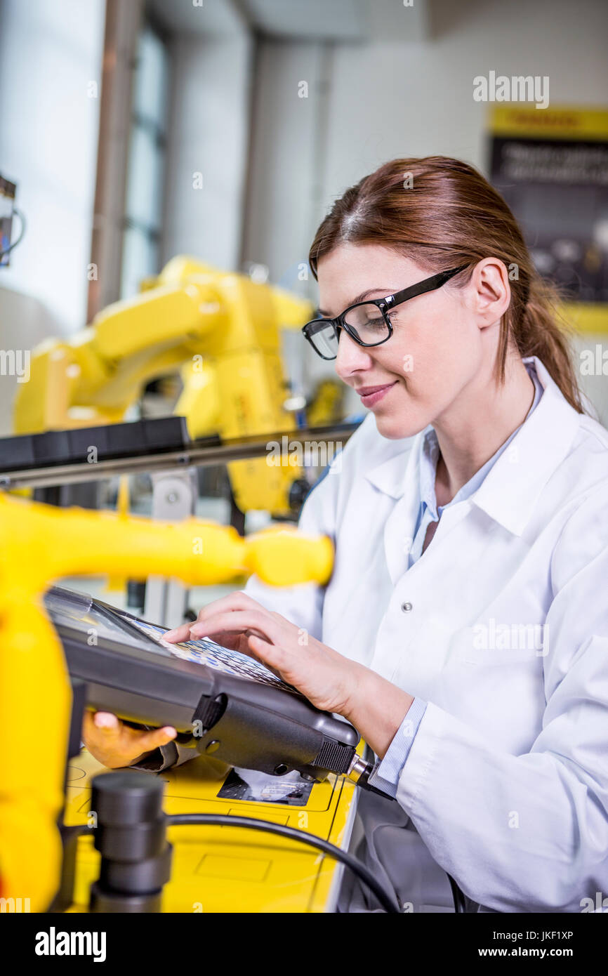 Woman using device in factory with industrial robots Stock Photo - Alamy