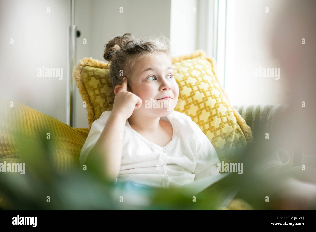 Portrait of thinking little girl sitting with magazine on armchair ...
