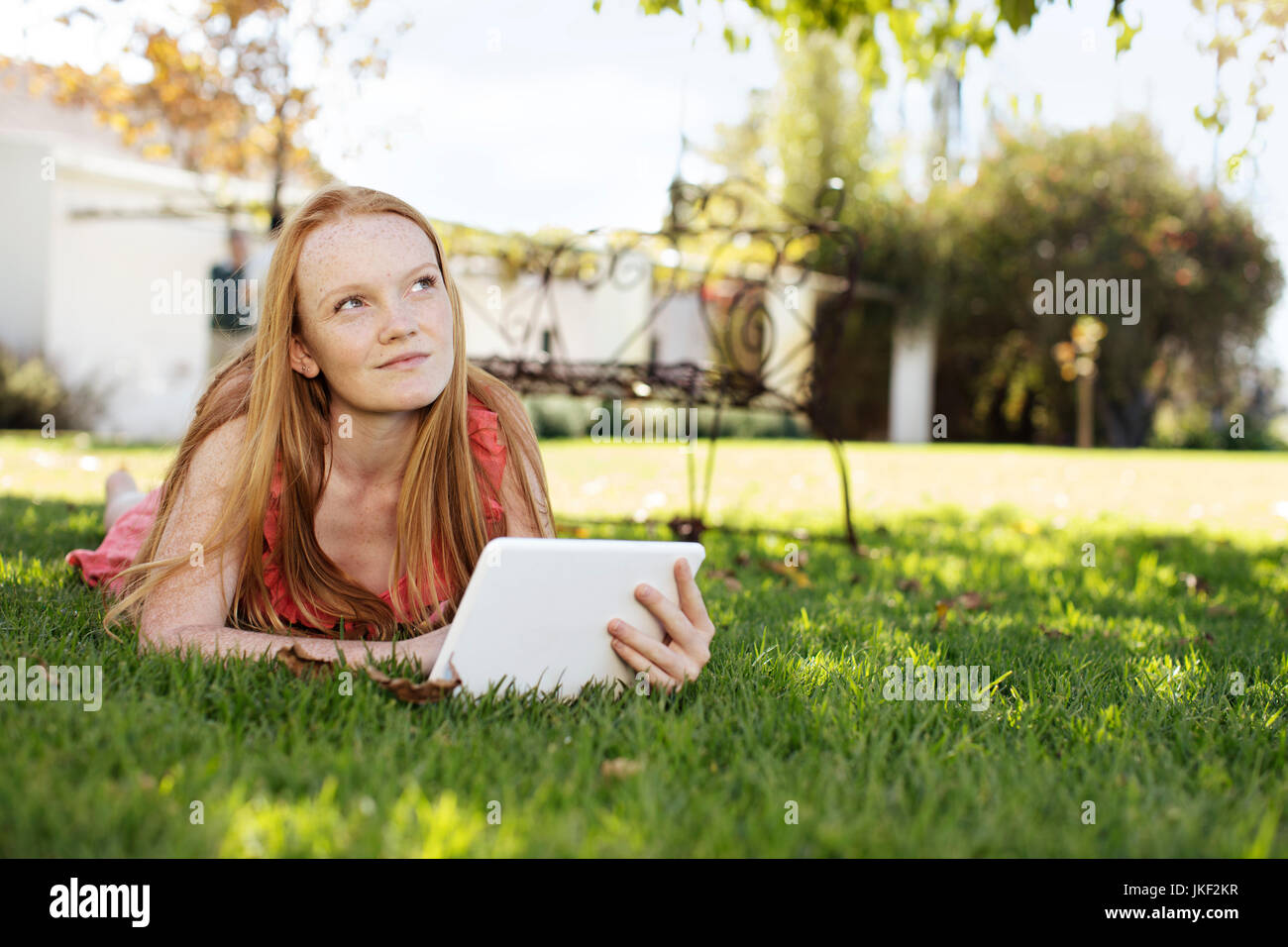 Grl with long red hair lying in grass with tablet Stock Photo - Alamy