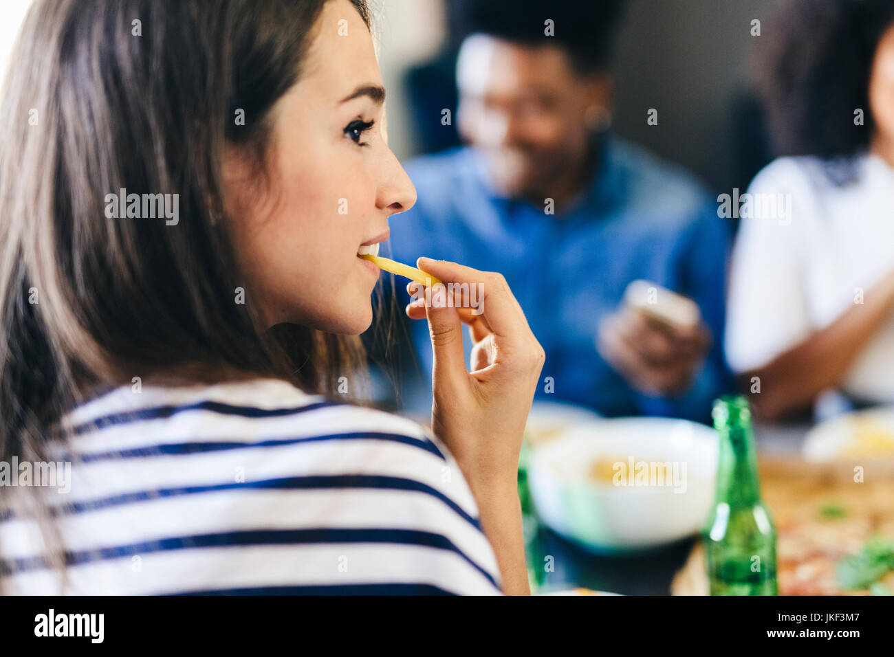 Woman eating French fry with friends in background Stock Photo - Alamy