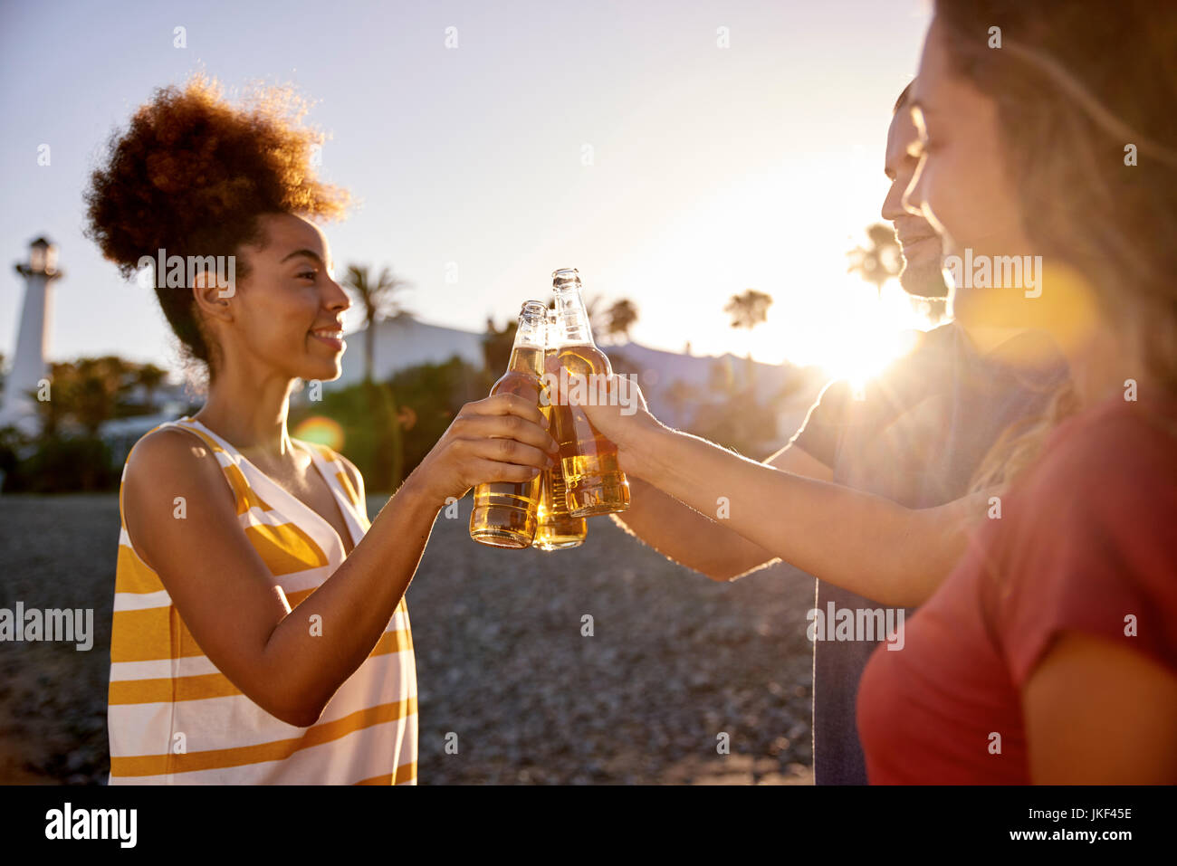 Three friends toasting with beer bottles on the beach at sunset Stock ...