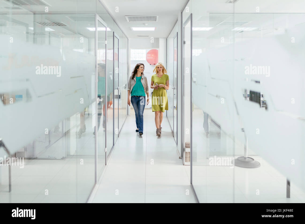 Two female colleagues walking in office corridor Stock Photo - Alamy