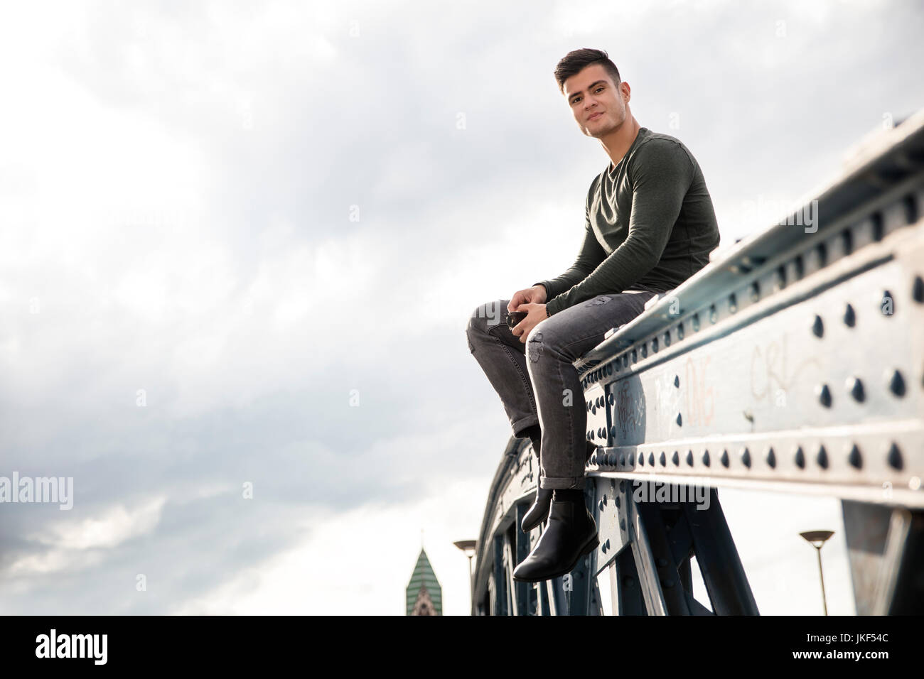 Young man sitting on railing of a bridge Stock Photo - Alamy