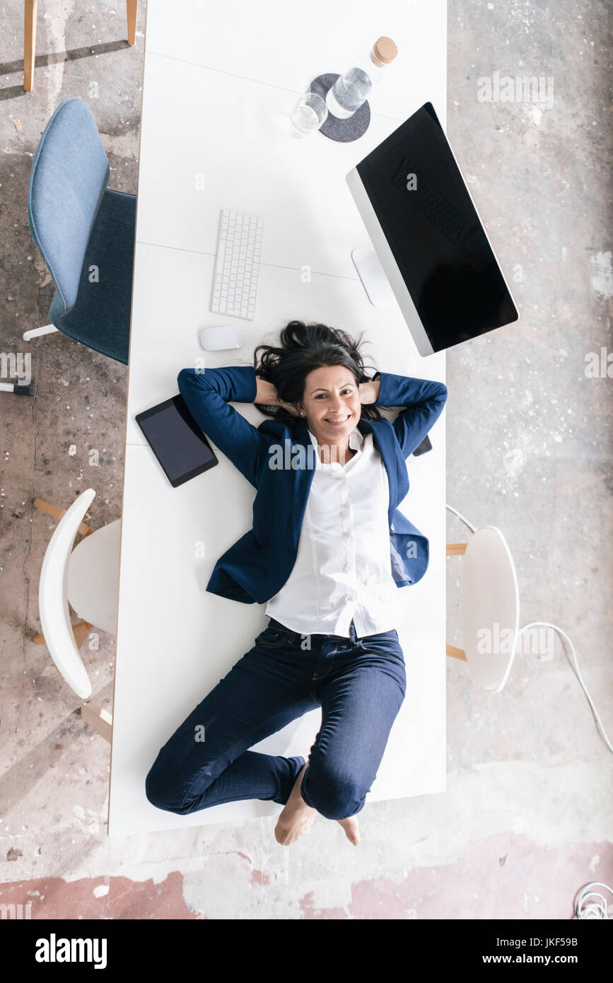 Portrait of smiling businesswoman lying on desk in the office Stock ...