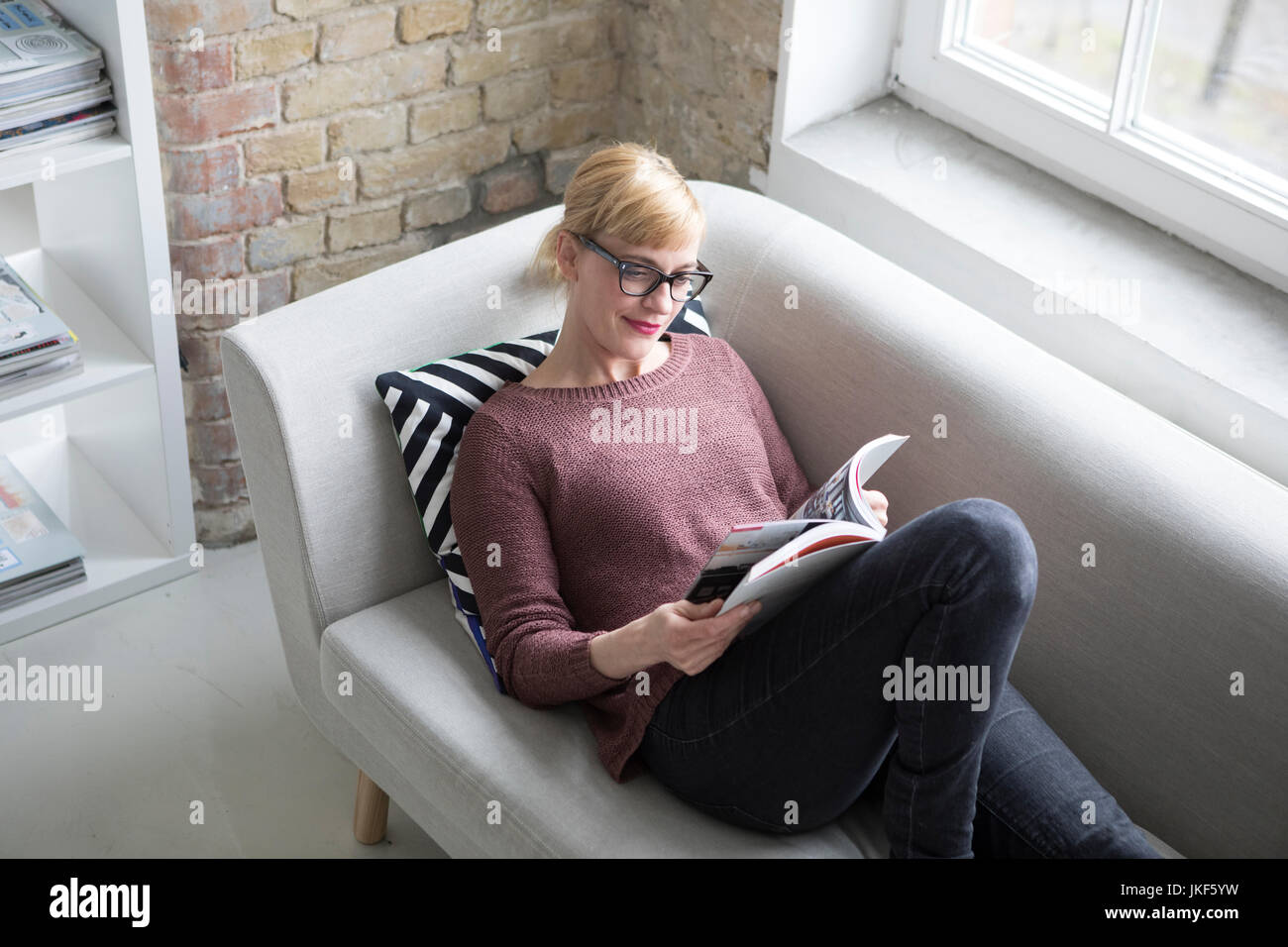 Woman sitting on couch, reading book Stock Photo - Alamy