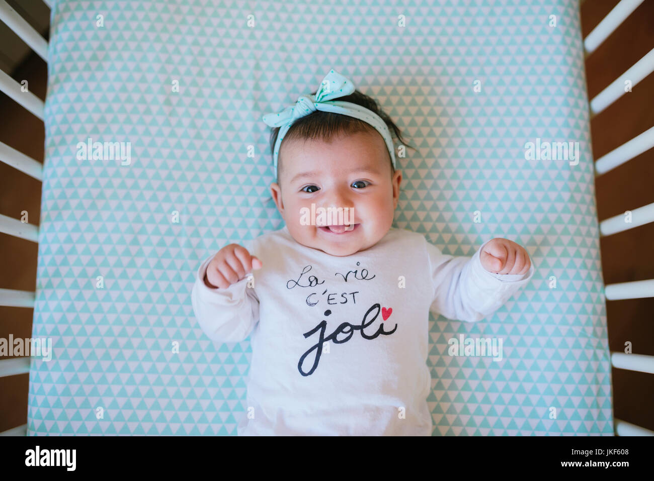 Happy baby girl with a hair ribbon lying in crib Stock Photo - Alamy