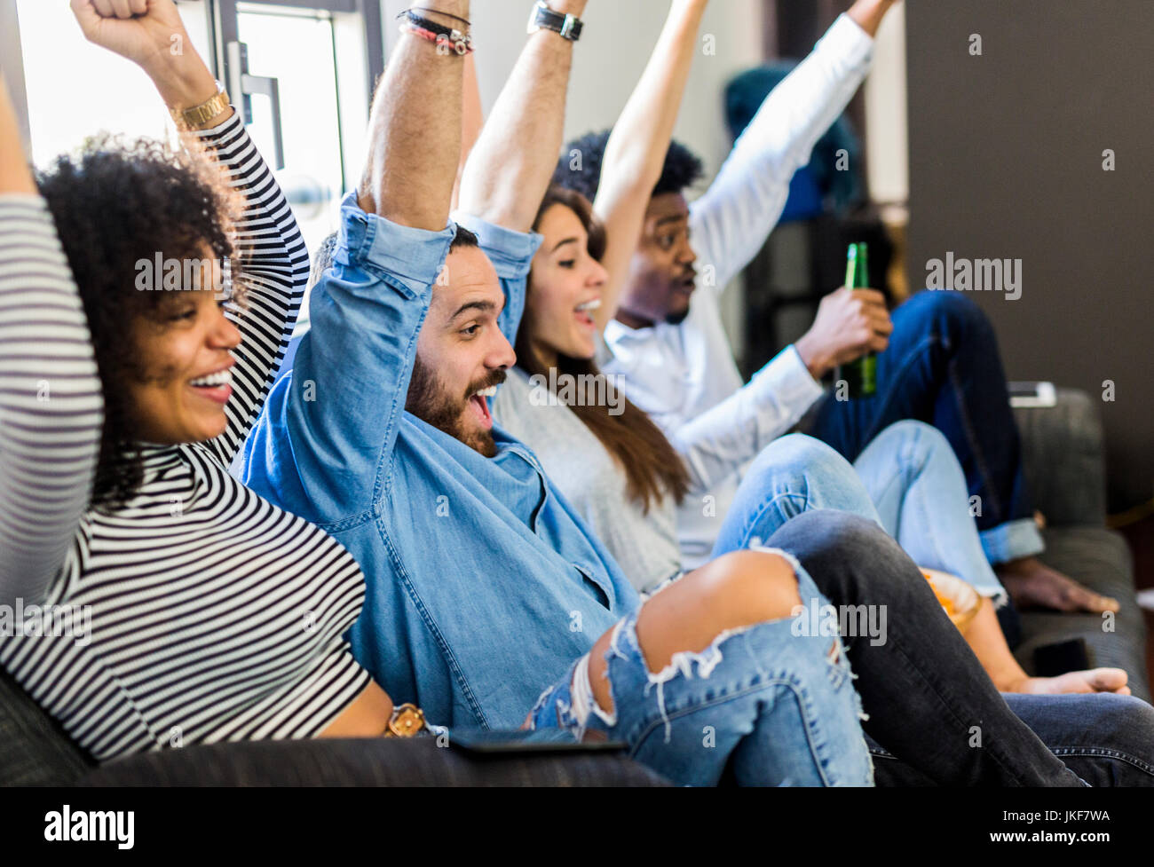 Excited friends sitting on the sofa raising their arms Stock Photo - Alamy