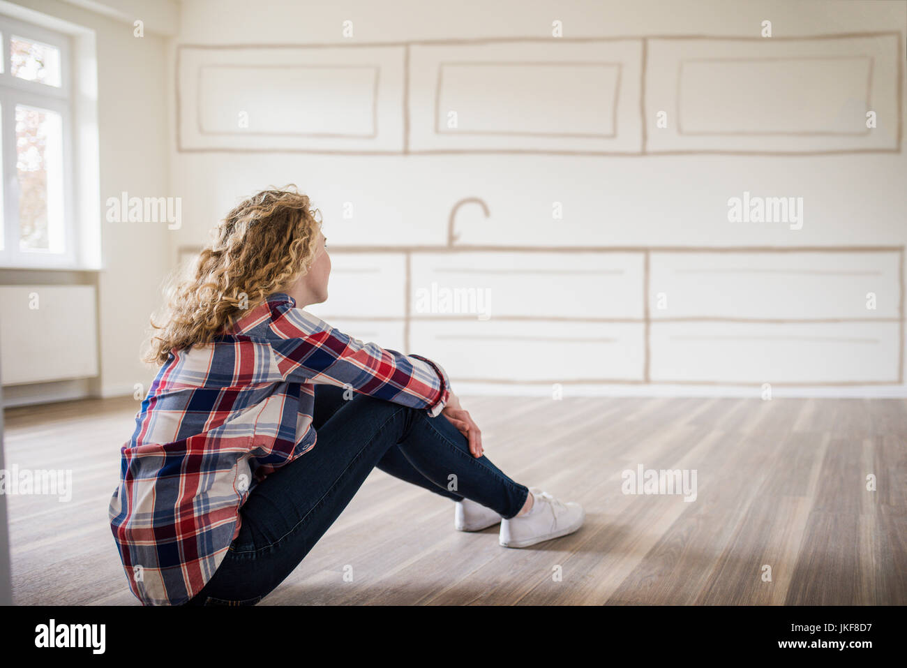 Young woman in new home sitting on floor thinking about interior design ...