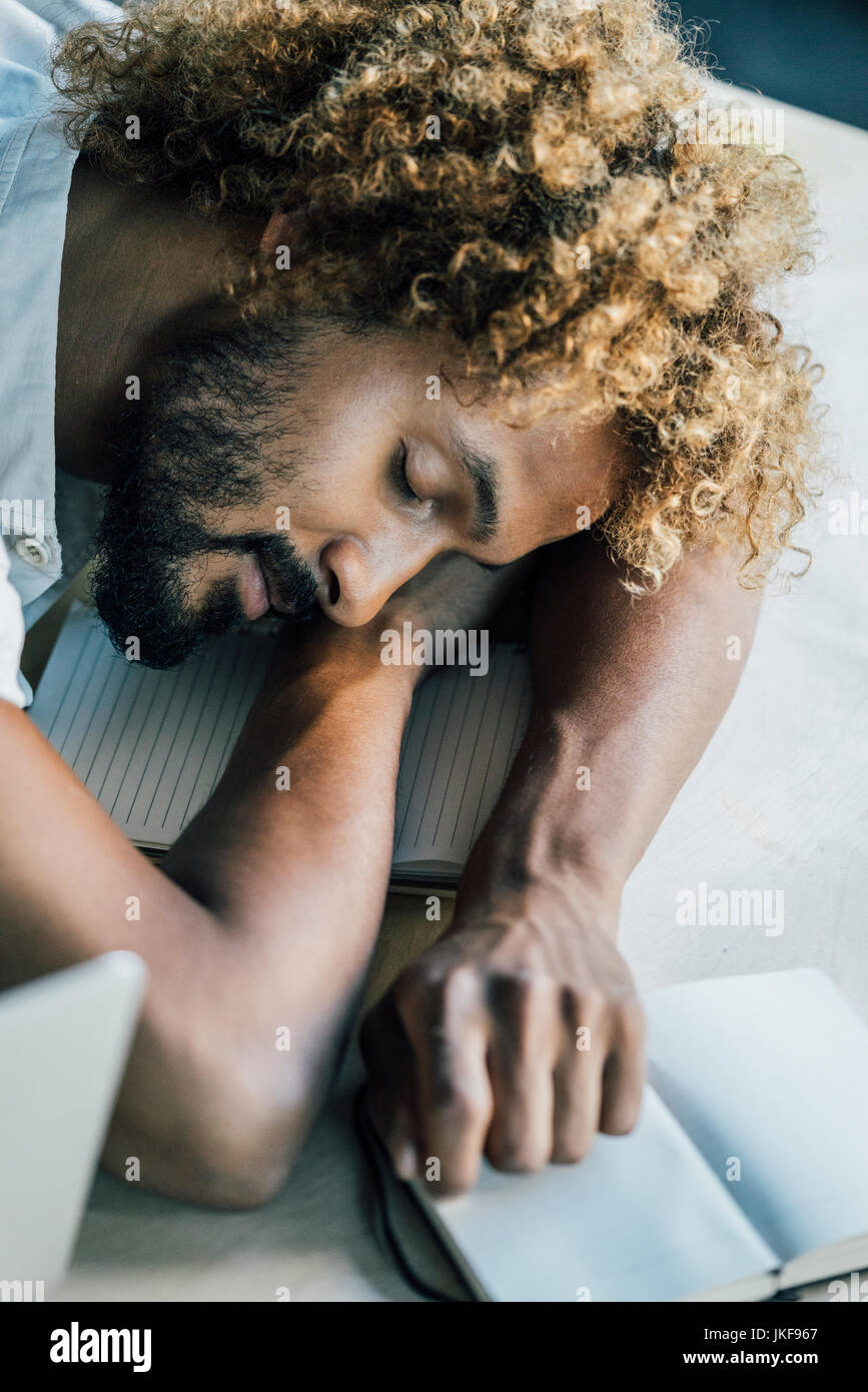 Young man lying on desk sleeping Stock Photo - Alamy