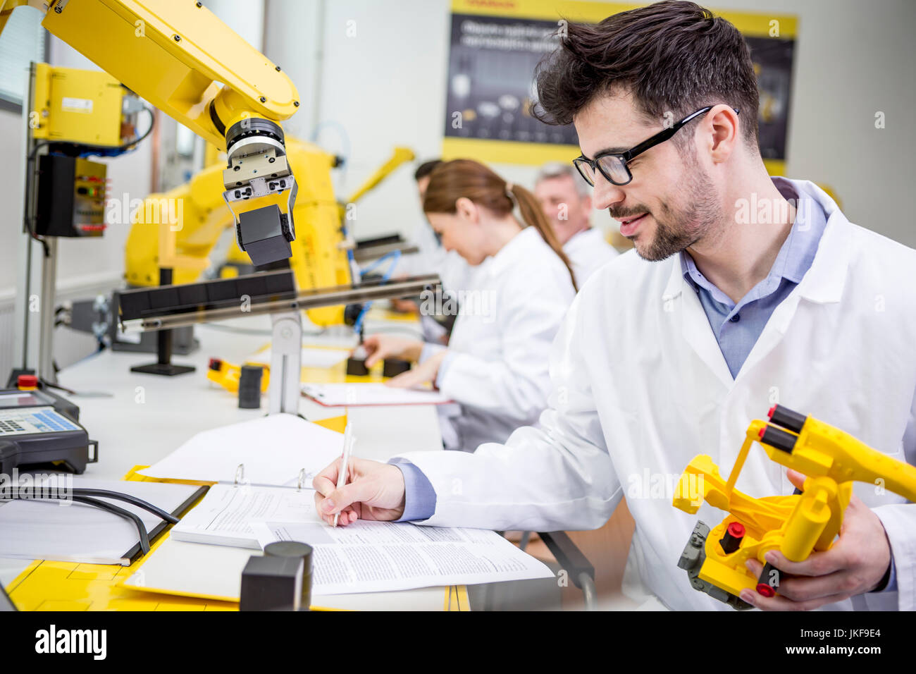 Engineer in factory holding model of an industrial robot taking notes ...