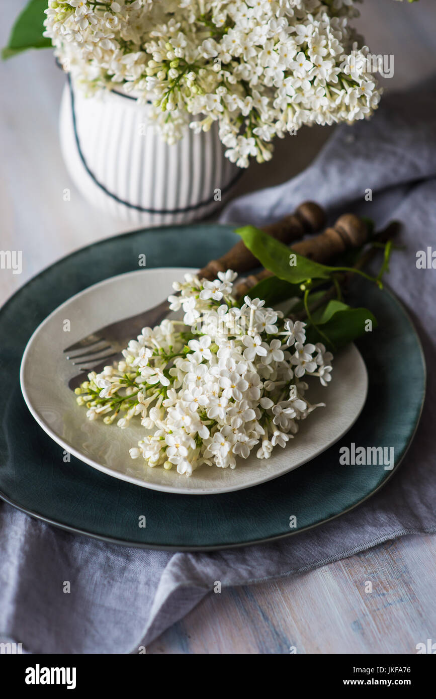 Pring Table Setting With White Lilac Flowers On The Plate With Flatware On Rustic Wooden Table
