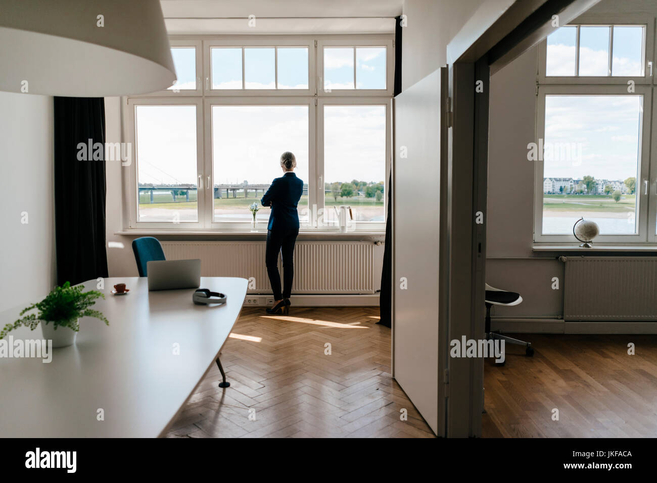 Businesswoman standing in modern office looking out of window Stock ...