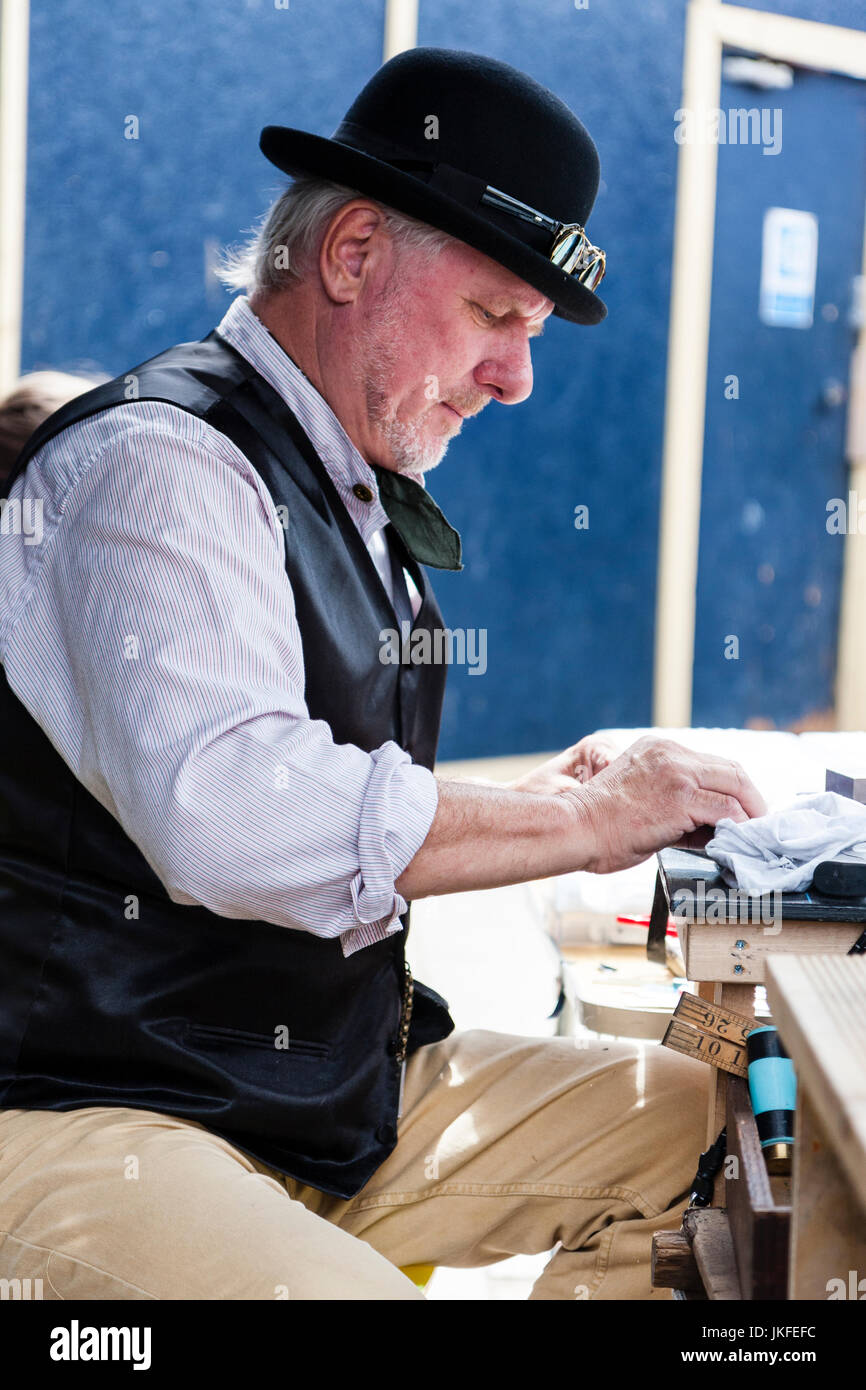 Mature man, 50s, sitting outdoors at work bench, he wears a waistcoat ...