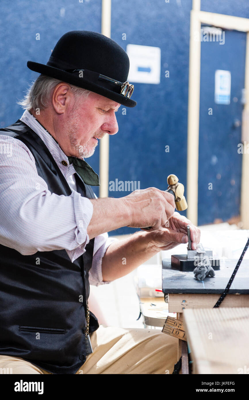 Mature man, 50s, sitting outdoors at work bench, he wears a waistcoat ...