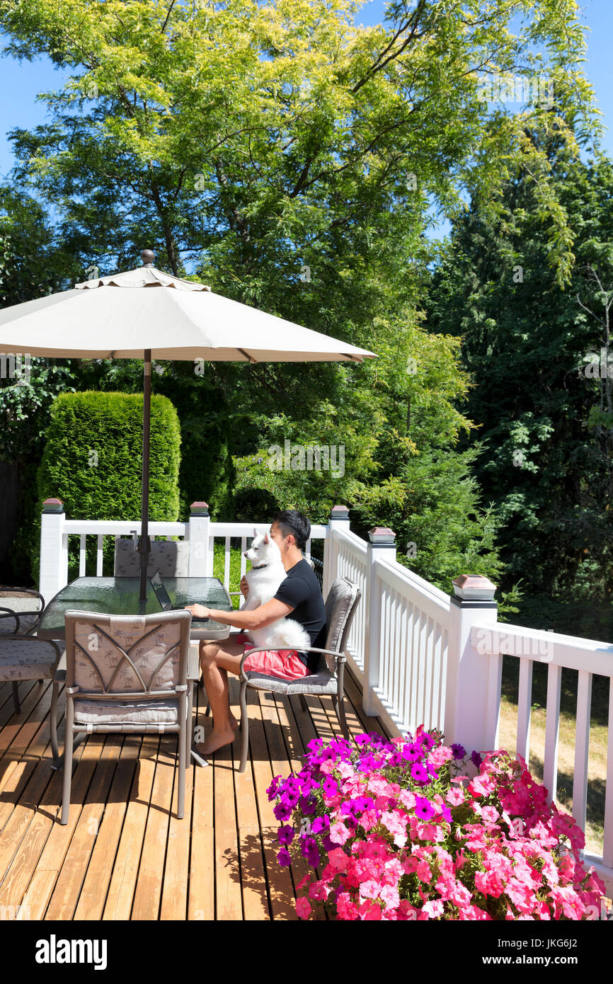 Young man working from home on outdoor cedar deck with computer and his ...