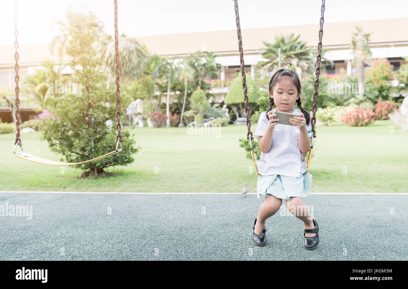 cute girl student play smart phone on swing in school playground Stock ...