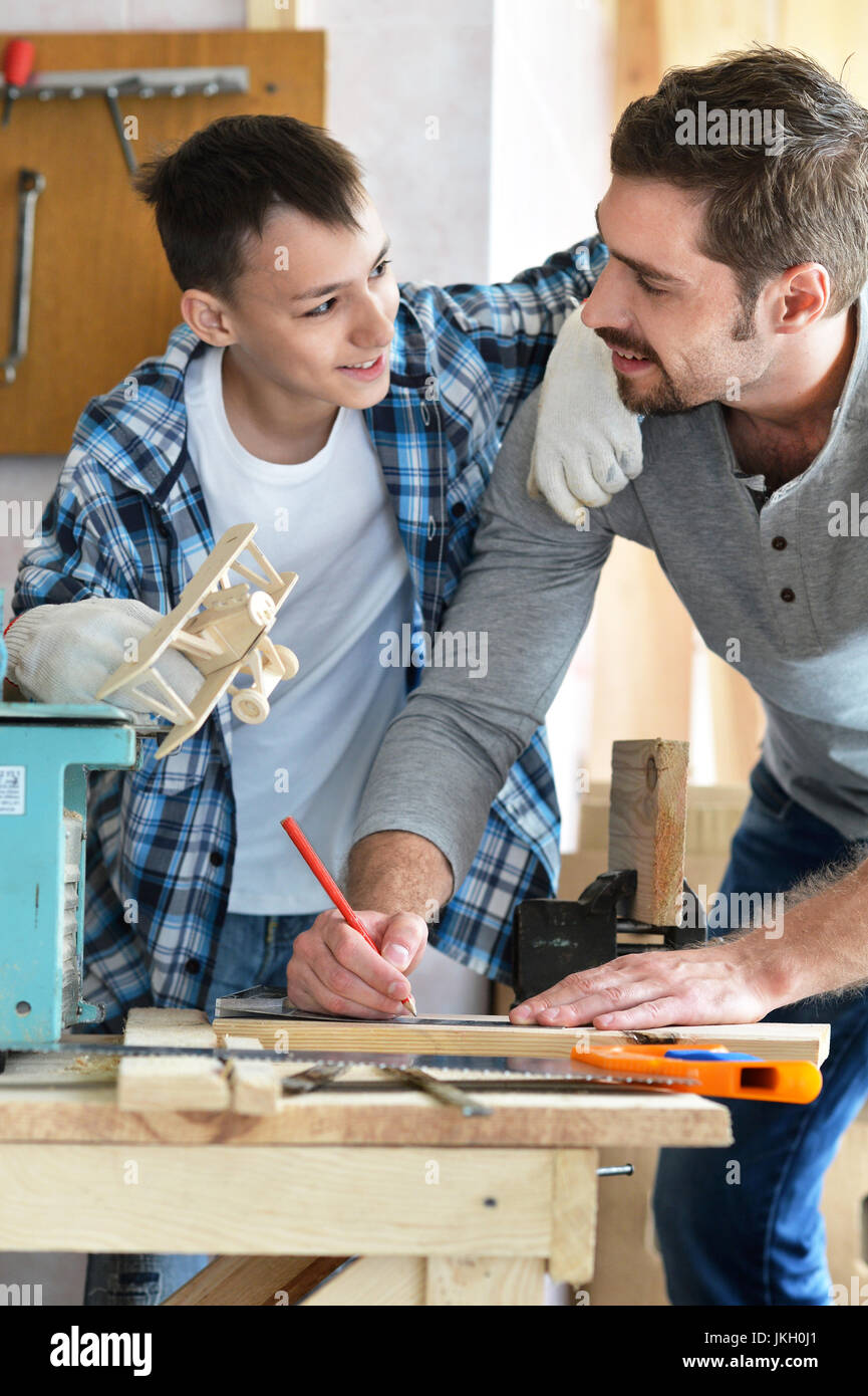 happy father and son processing wood in carpentry workshop Stock Photo ...