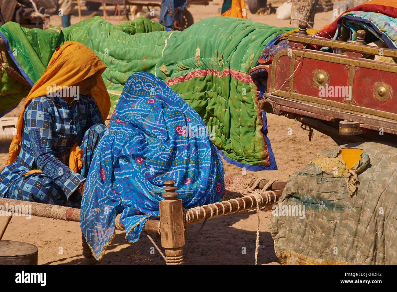 Women in brightly coloured clothing sitting on a bed, known as a ...