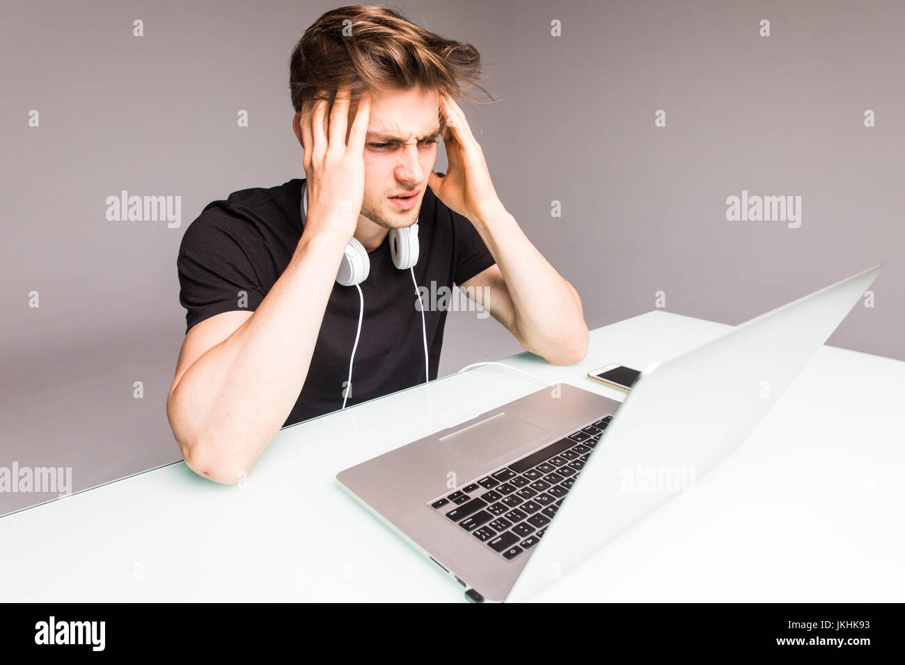 Handsome young man suffering from headache while working with laptop on ...