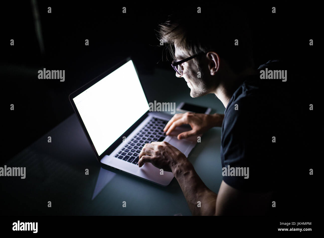 Young concentrated man using laptop computer at home indoors at night ...