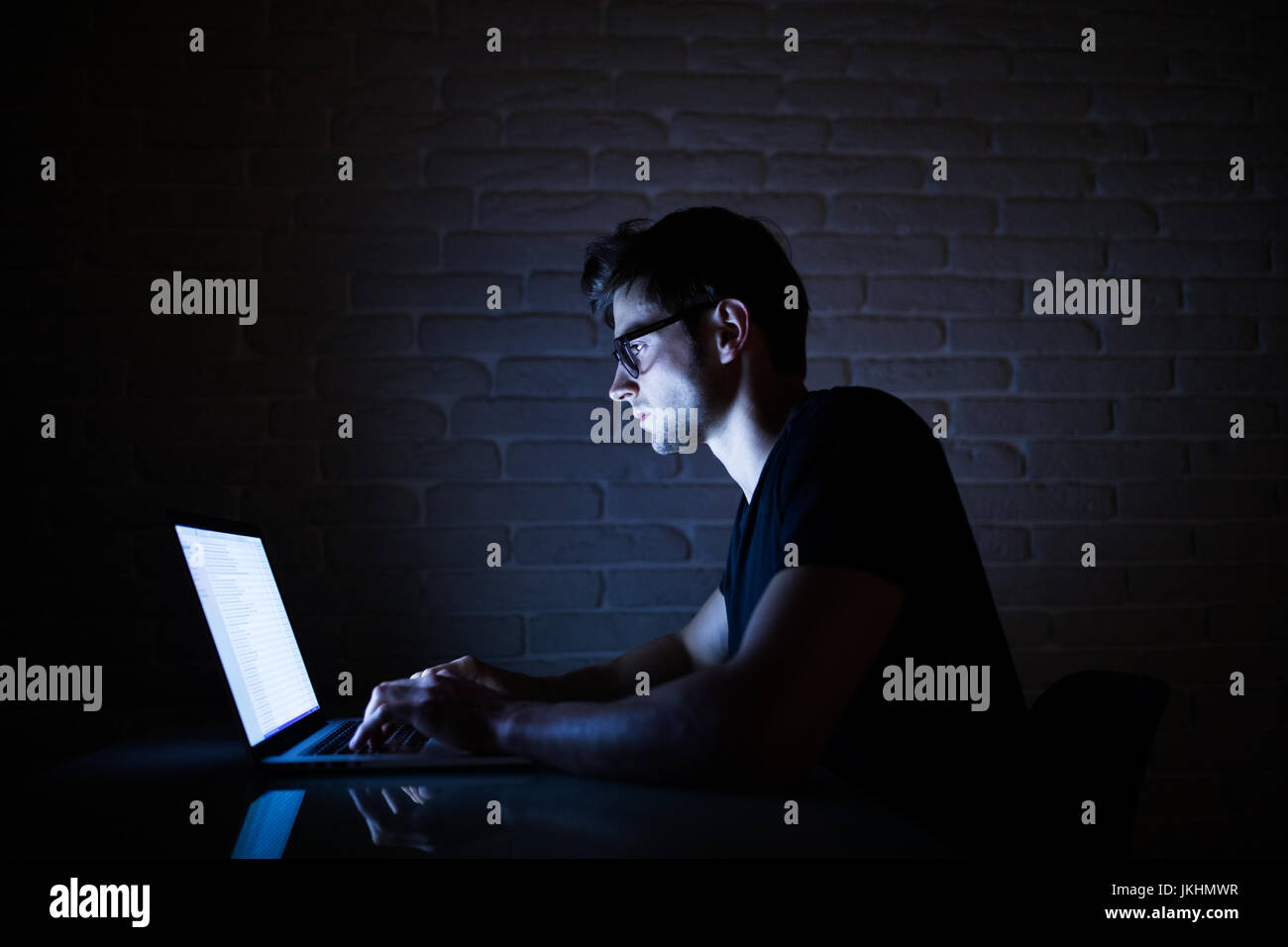 Young man working on computer at night in dark office. The designer ...