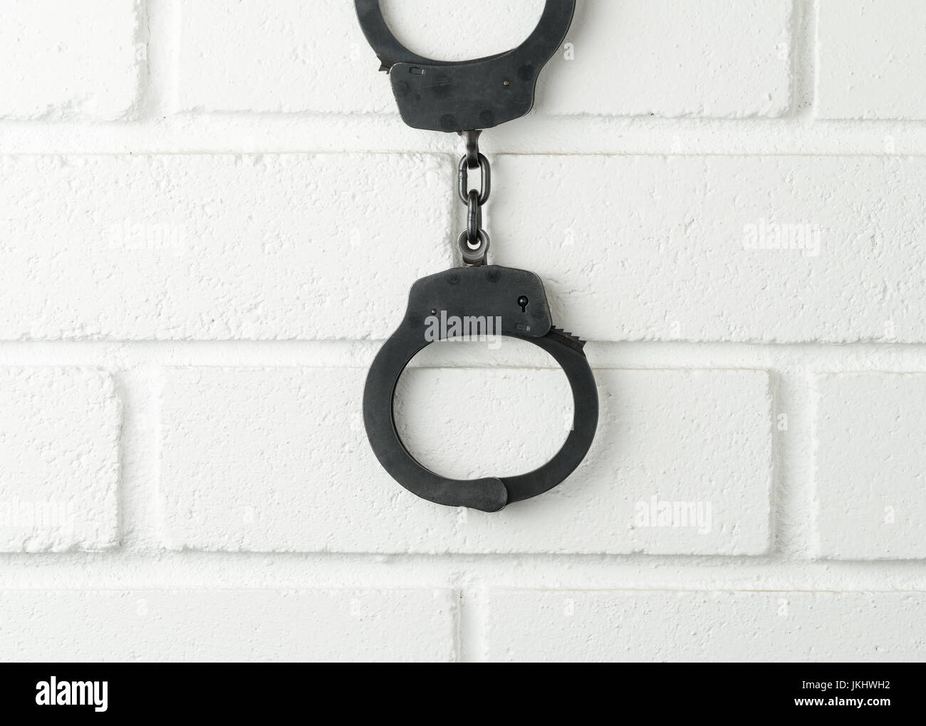 Police handcuffs on white painted brick wall Stock Photo - Alamy