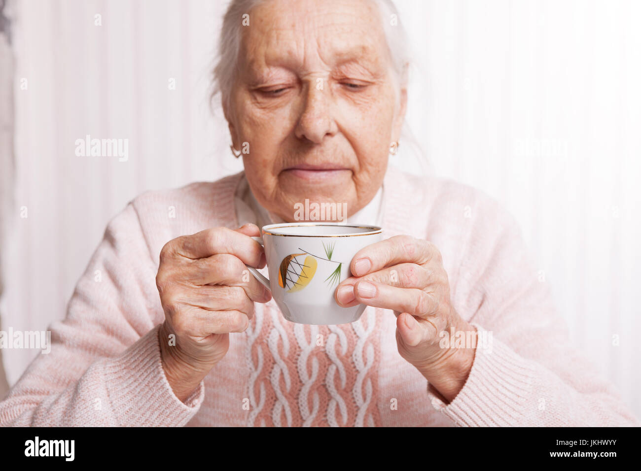 An elderly woman drinks tea at home. Senior woman holding cup of tea in ...