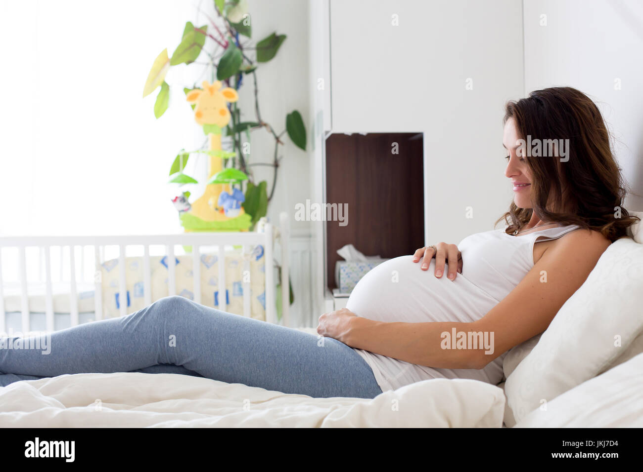 Happy young beautiful pregnant woman, sitting on bed in bedroom ...