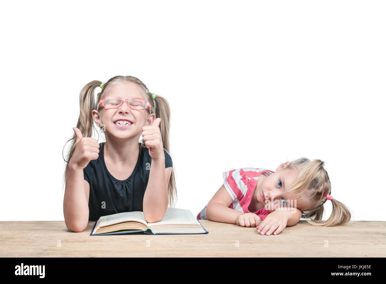 Two girls sitting at a table behind a book with different emotions ...