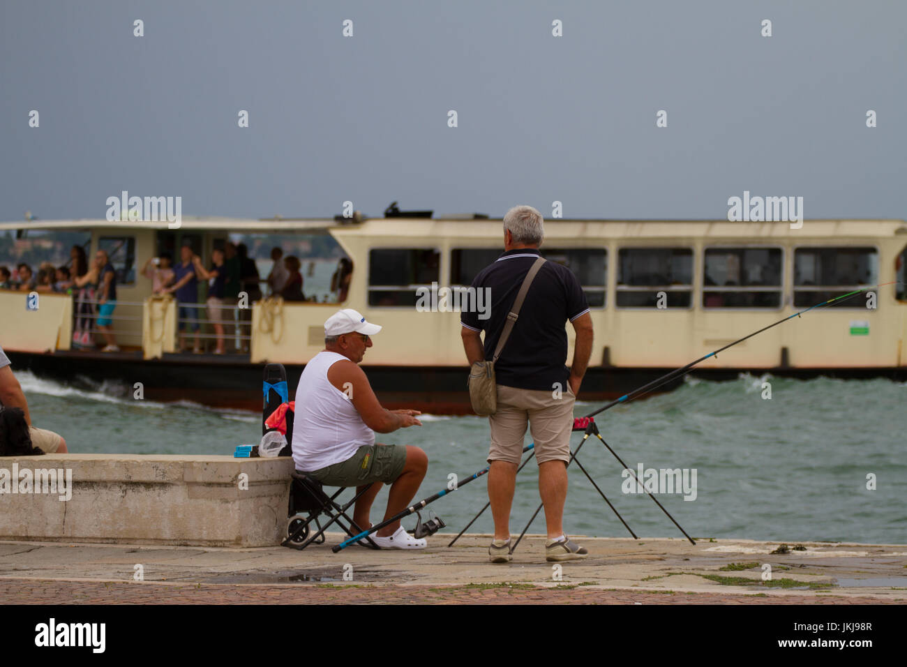 Man fishing on quayside, and bystander. Venice, Italy Stock Photo - Alamy