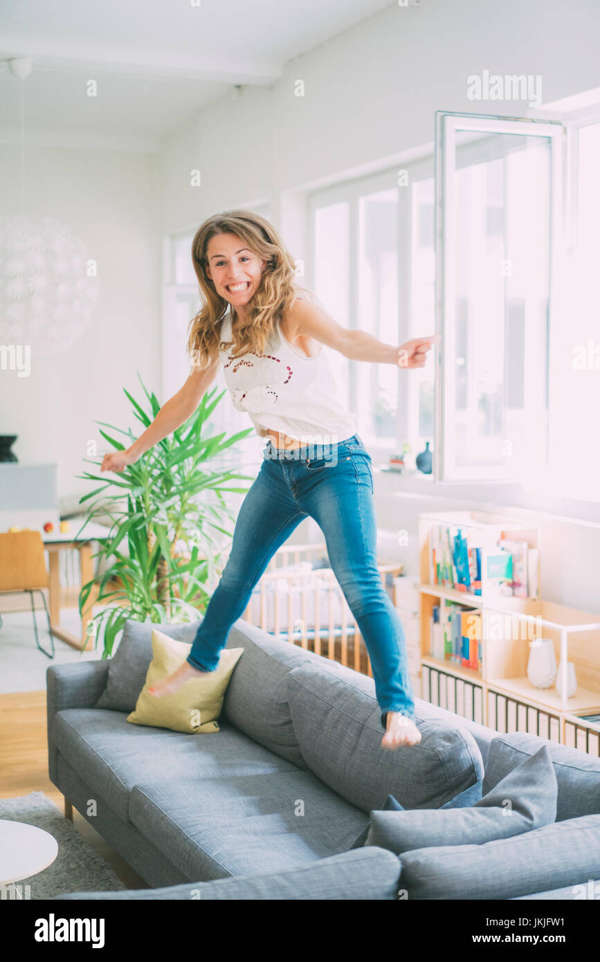 Excited young woman jumping on couch at home Stock Photo - Alamy