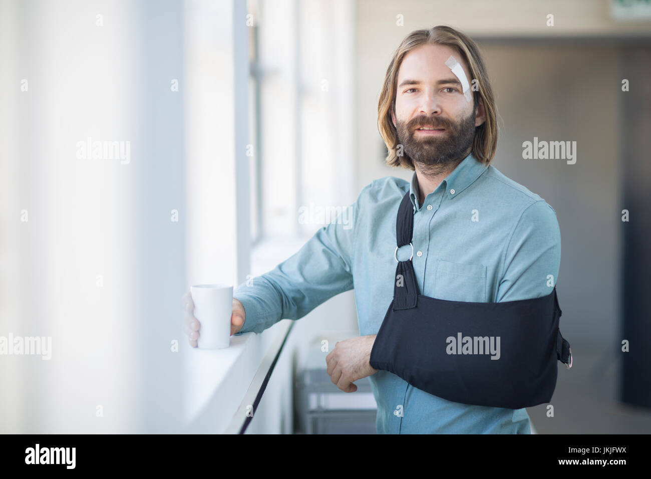 Employee with sling standing by the window Stock Photo - Alamy