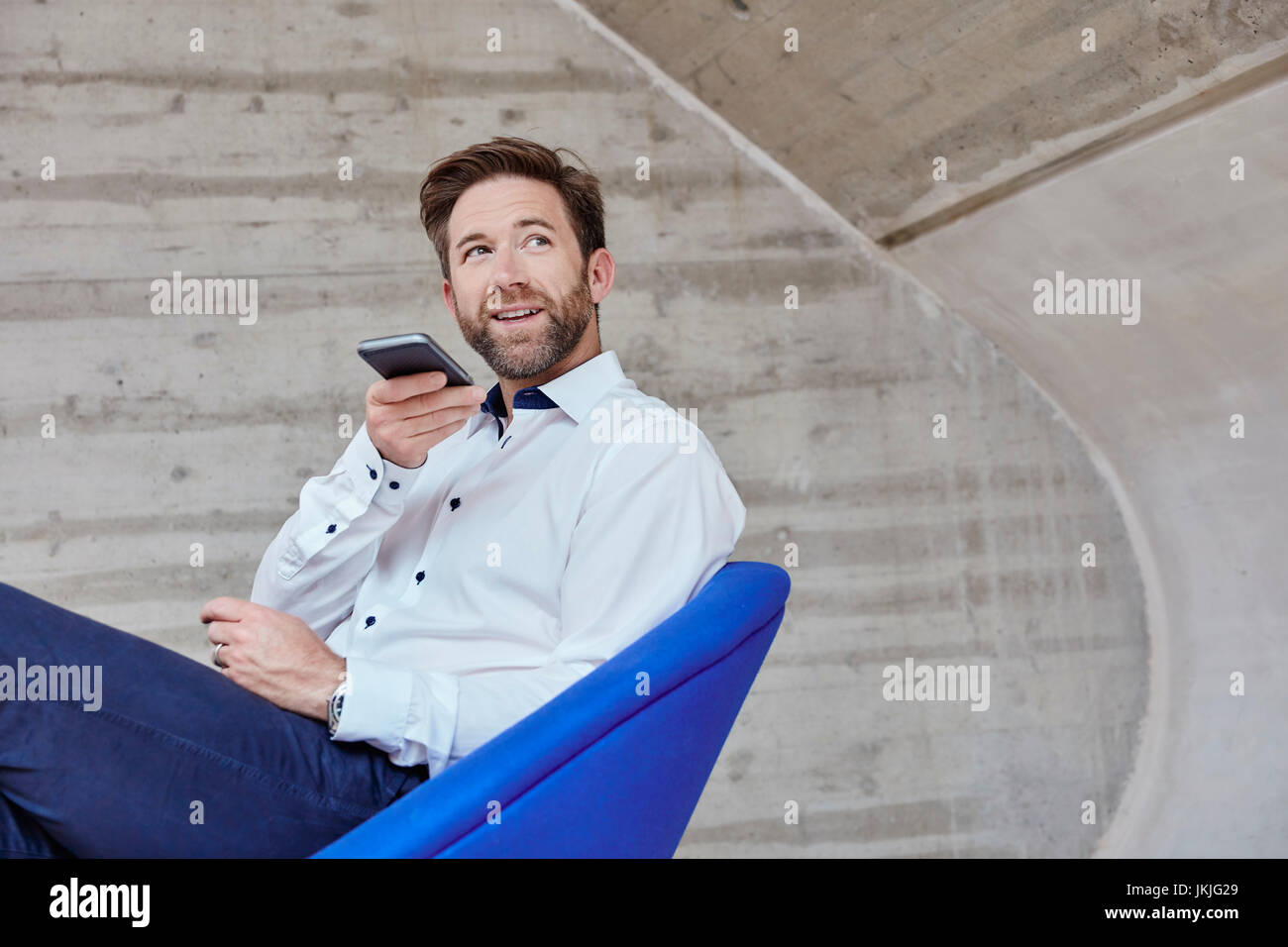 Businessman sitting on chair using cell phone Stock Photo - Alamy