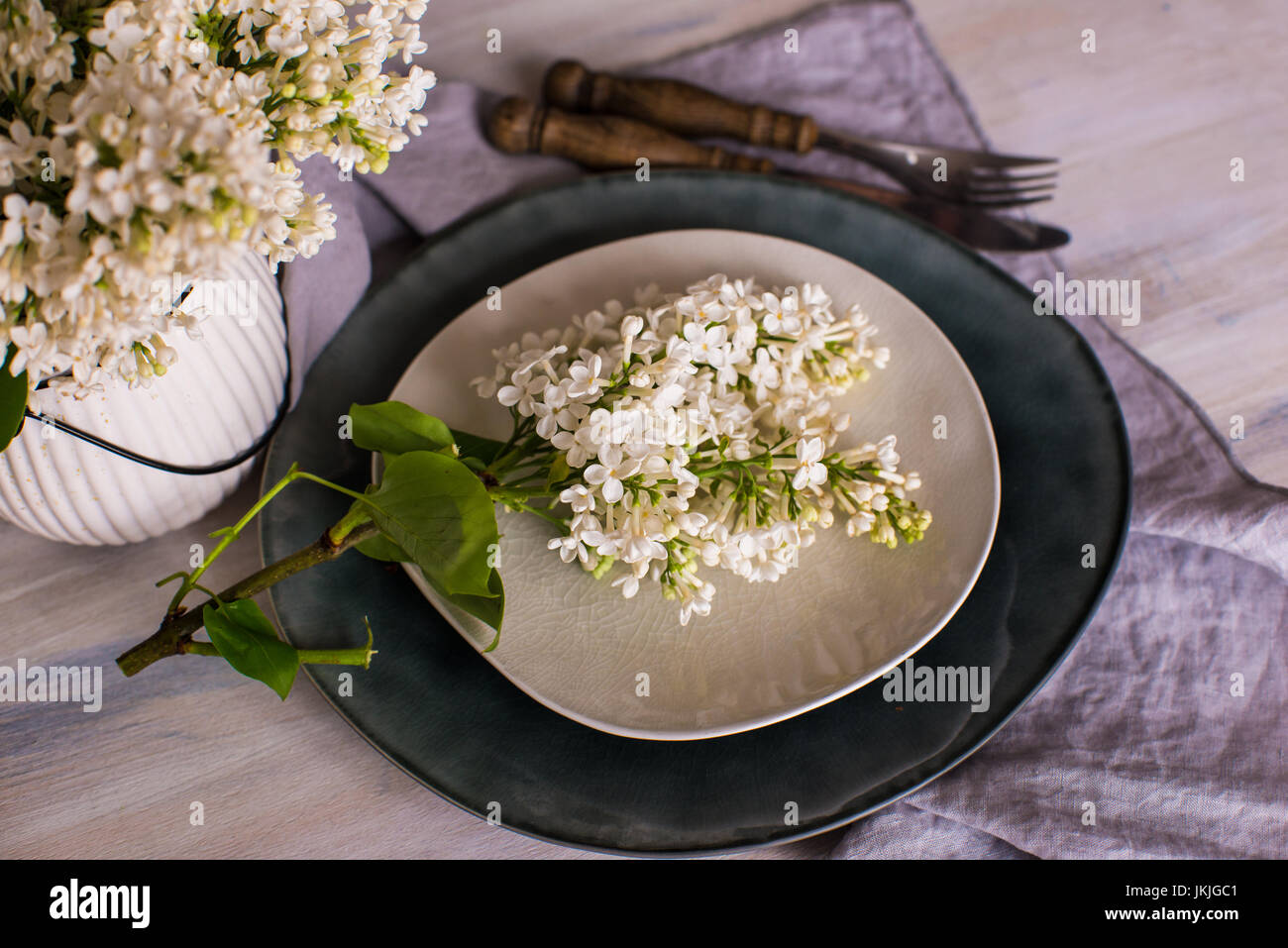 Pring Table Setting With White Lilac Flowers On The Plate With Flatware On Rustic Wooden Table